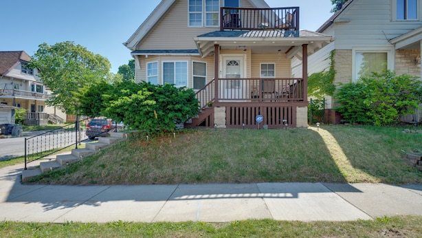 A two-story house with a front porch, a small balcony, and a driveway leading to a parked car.