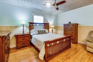Um quarto com uma cama de madeira, duas mesas de cabeceira, um penteado, um ventilador de teto e uma janela com persianas.