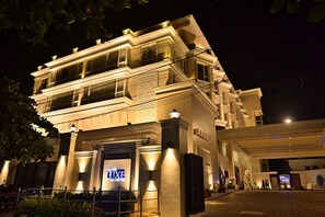 Entrada de hotel com uma placa visível, um portão na entrada e fachada bem iluminada.
