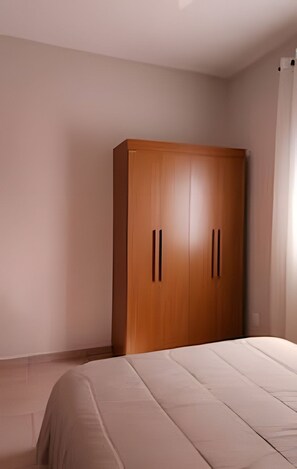 Quarto com um grande armário de madeira, uma cama com colchão branco e uma parede lisa.
