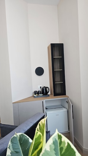Quarto compacto com cozinha compacta, pequena geladeira, máquina de café e espelho redondo na parede.