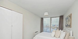 Quarto com cama grande, armário, janela com cortinas e vista para a cidade.