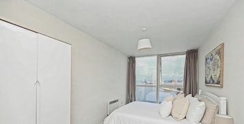 Quarto com cama grande, armário, janela com cortinas e vista para a cidade.