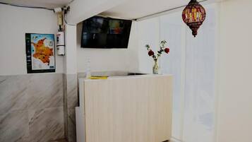 Uma área de recepção com parede de mármore, balcão de madeira, TV fixada na parede e luminária pendente decorativa.