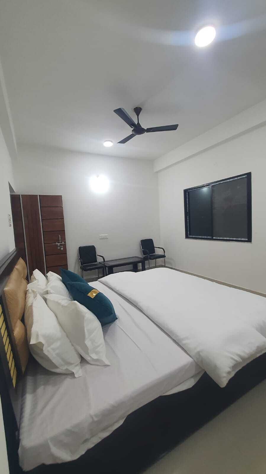 Quarto de hotel com cama, escrivaninha, cadeira, guarda-roupa e ventoinha no teto.