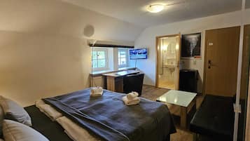 Quarto de hotel com cama, escrivaninha, televisão, espelho e banheiro.