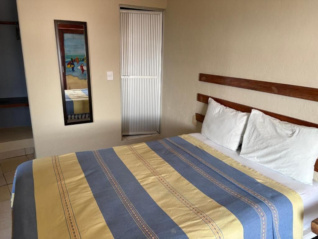 Quarto de hotel com cama, janela com persianas, porta e espelho fixado na parede.
