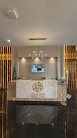 Um balcão de recepção de hotel com tampo de mármore, uma televisão montada e um lustre moderno.