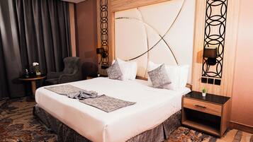 Quarto de hotel com uma cama grande, uma cadeira, uma mesa de cabeceira e uma luminária de parede.
