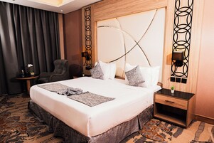 Quarto de hotel com uma cama grande, uma cadeira, uma mesa de cabeceira e uma luminária de parede.
