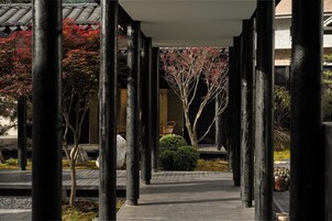 Um corredor tradicional em estilo japonês, com pilares de madeira, telhado de telhas e um caminho que leva a um edifício.