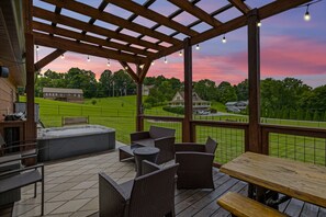 Um alpendre coberto com móveis de vime, uma banheira de hidromassagem e vista para uma paisagem verde.