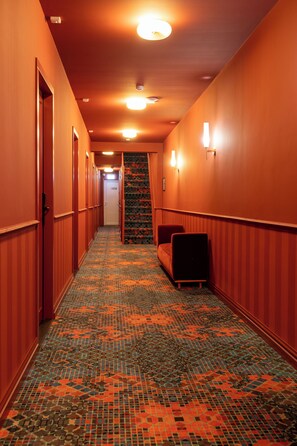Um corredor de hotel com carpete estampado, um sofá e uma porta no final.