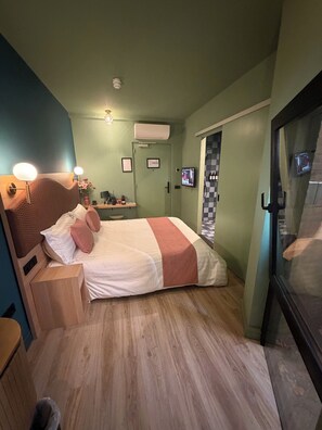 Quarto com cama, mesa de cabeceira, luminária, ar condicionado e televisão na parede.