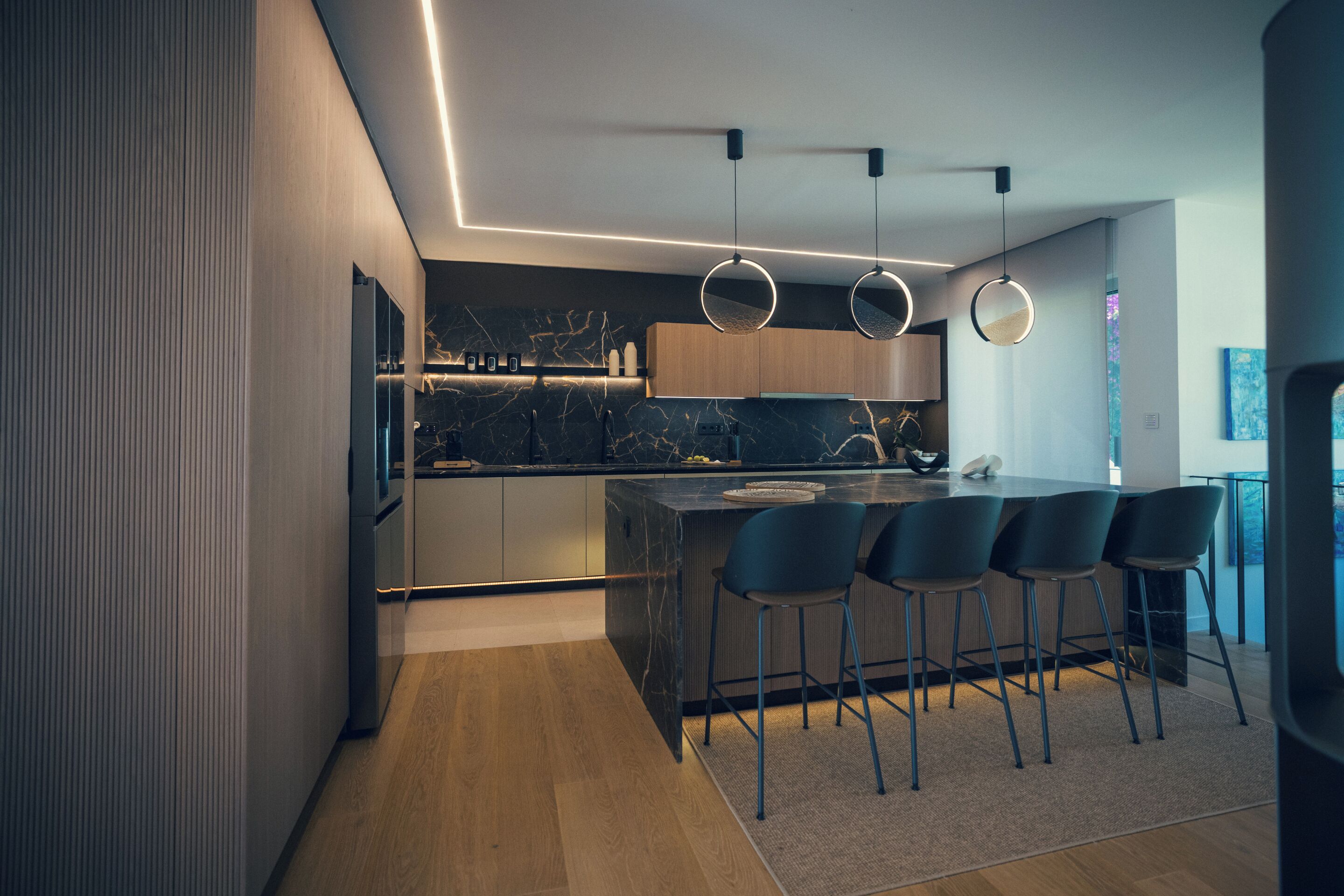 Uma cozinha moderna com bancada de mármore, banquetas e iluminação pendente.