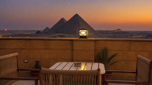 Um terraço com vista para as pirâmides, uma mesa com cadeiras e um candeeiro.