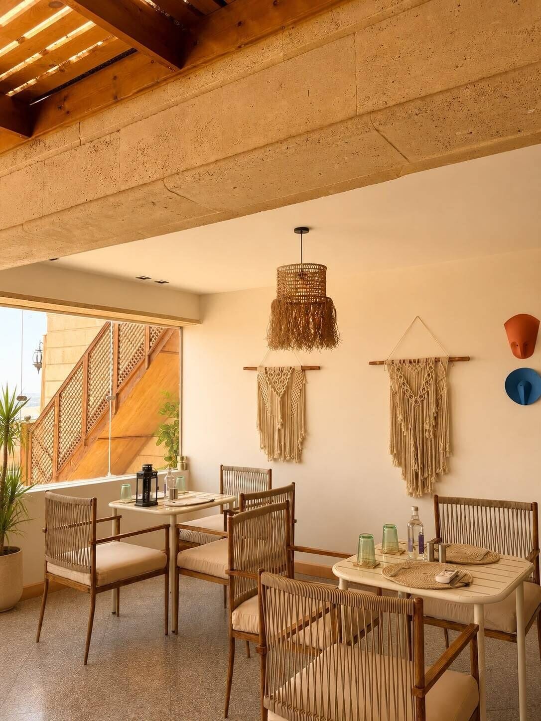 Uma área de refeições com mesa e cadeiras, um pendente de macramé na parede e uma escada.