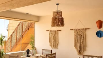 Uma área de refeições com mesa e cadeiras, um pendente de macramé na parede e uma escada.