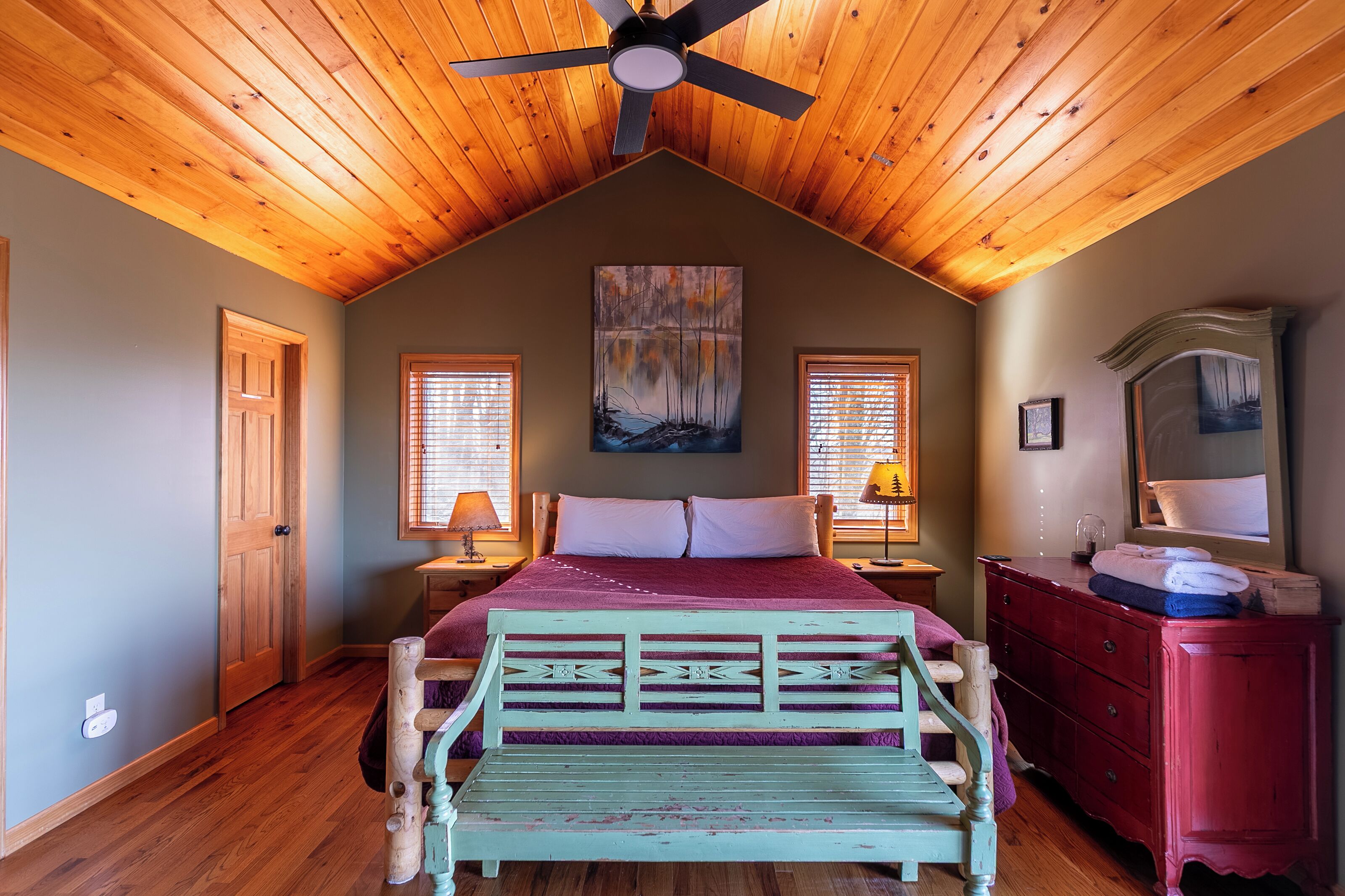Quarto com teto de madeira, cama com peseira, cômoda e um quadro na parede.