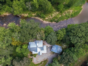 Vista aérea de uma casa rodeada por floresta densa, com um rio serpenteando ao lado da propriedade.