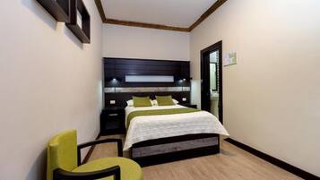 Quarto com cama, mesas de cabeceira, uma cadeira e prateleira na parede.