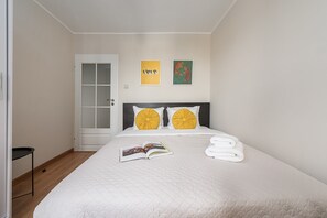 Uma cama bem arrumada com um edredom branco, duas almofadas com detalhes amarelos e um livro sobre a cama.