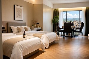 Quarto de hotel com duas camas, área de refeições e vista para as montanhas.