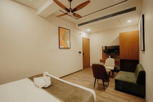 Quarto de hotel com cama, escrivaninha, cadeira, sofá, TV e ventilador de teto.