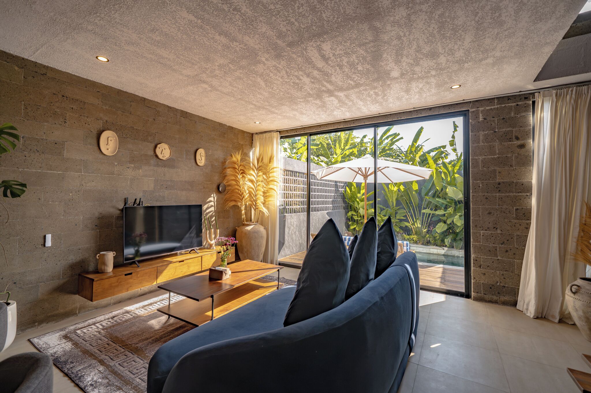 Uma sala de estar moderna com uma televisão de tela plana, um sofá, uma mesa de centro e uma janela grande com vista para áreas verdes.