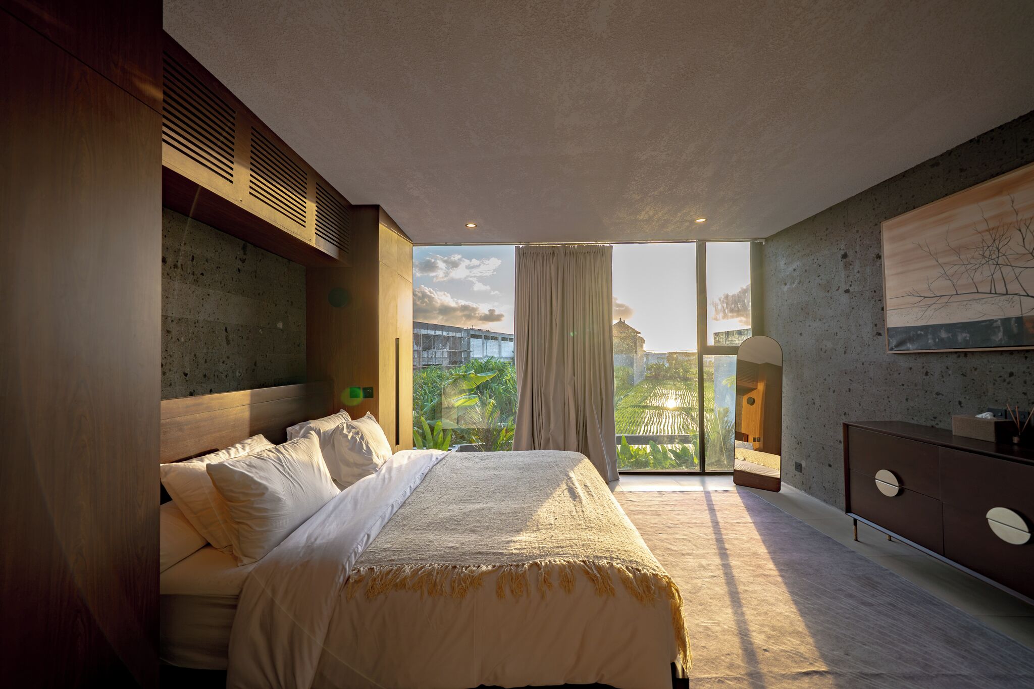 Quarto moderno com uma cama grande, vista para o verde, varanda e cômoda moderna.