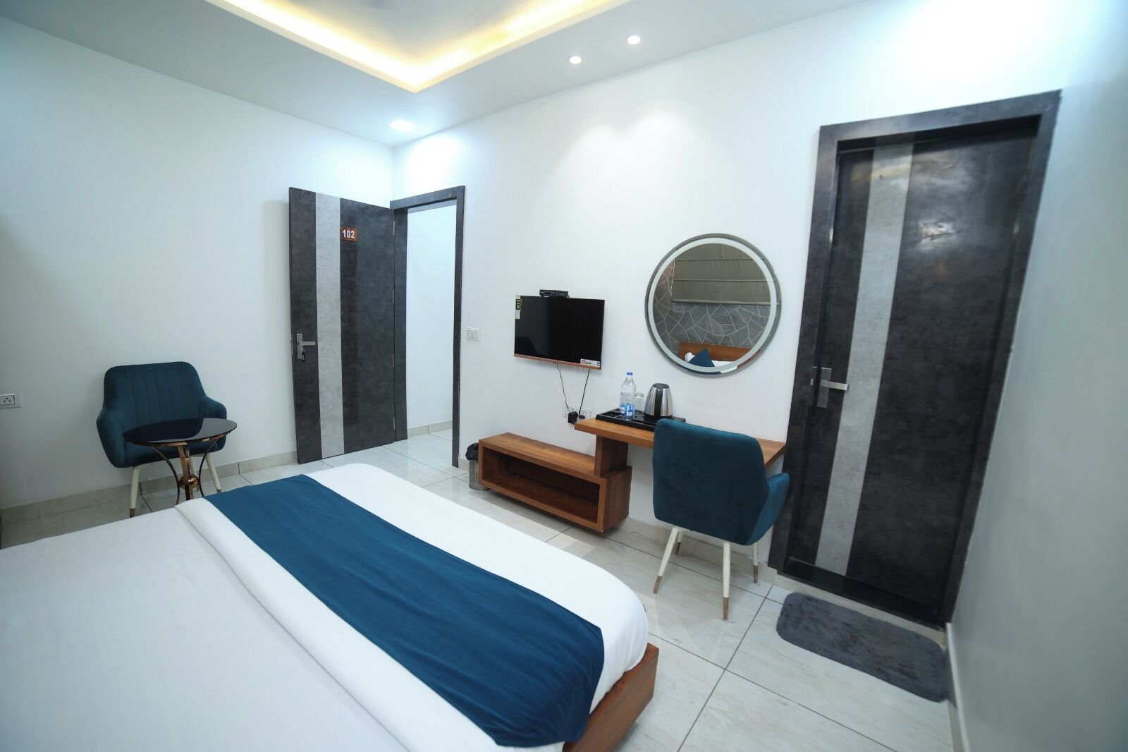 Quarto de hotel com cama, escrivaninha, cadeira, televisão e porta.