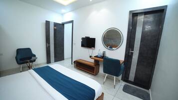 Quarto de hotel com cama, escrivaninha, cadeira, televisão e porta.