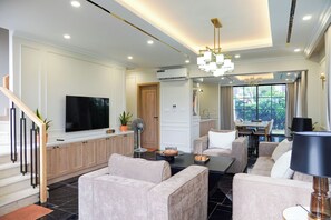 Uma sala de estar moderna com televisão de tela plana, assentos confortáveis, uma área de jantar e uma escada.