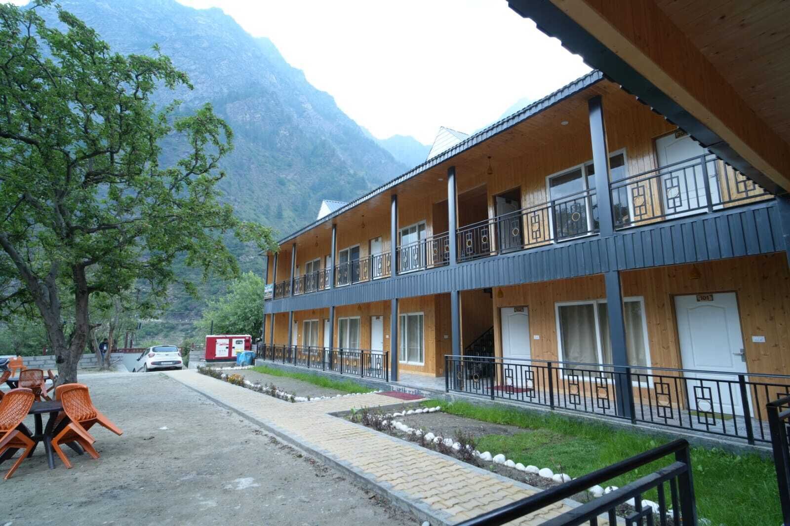 Um hotel com vários andares, varandas, um calçadão pavimentado e montanhas ao fundo.