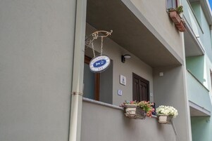 Um edifício com varanda, uma placa pendurada e floreiras.