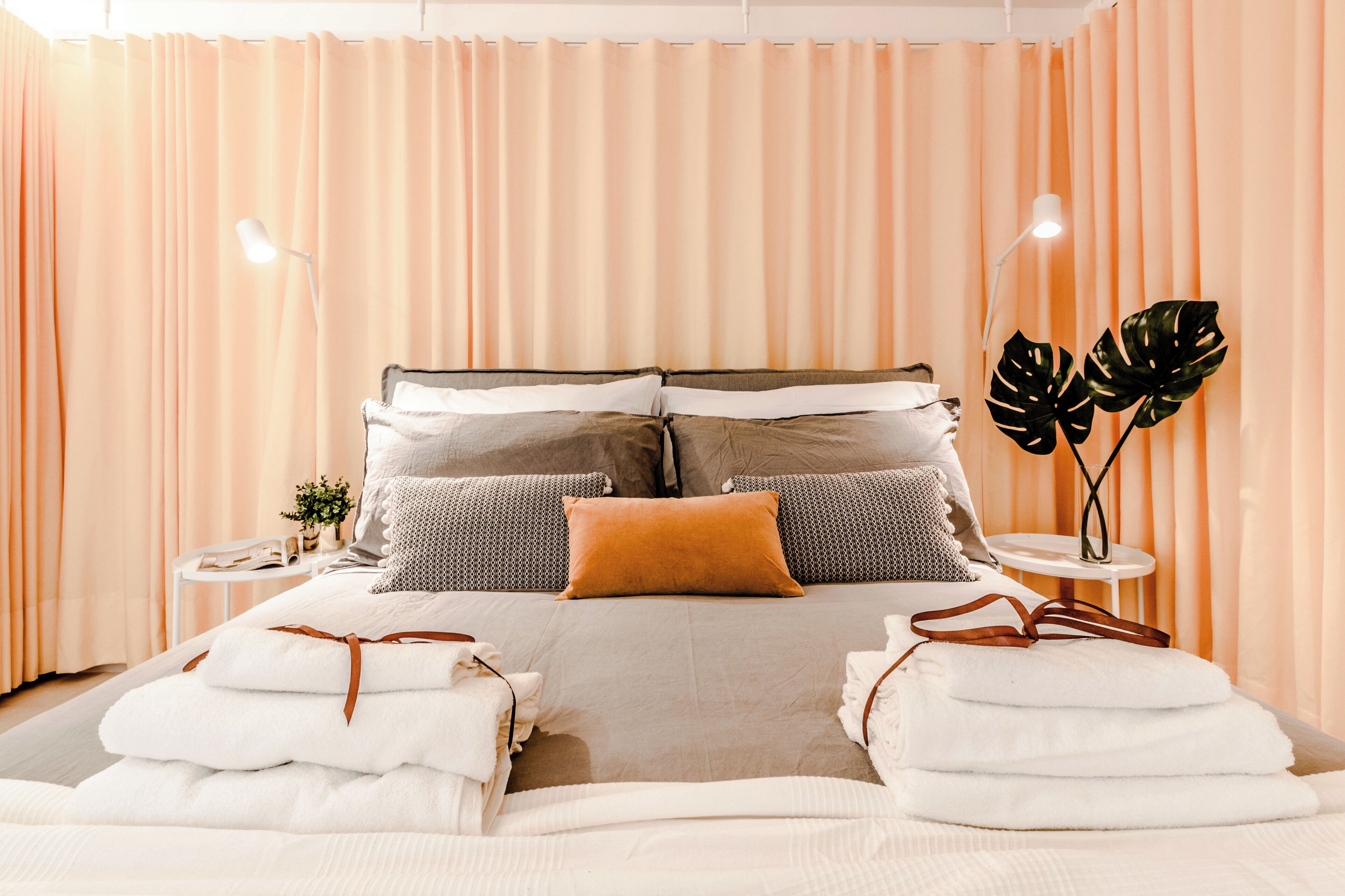 Cama bem arrumada com várias almofadas e mesa de cabeceira com uma planta.