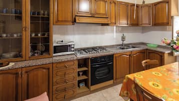 Uma cozinha com armários de madeira, fogão, forno e uma mesa de jantar com toalha de mesa florida.