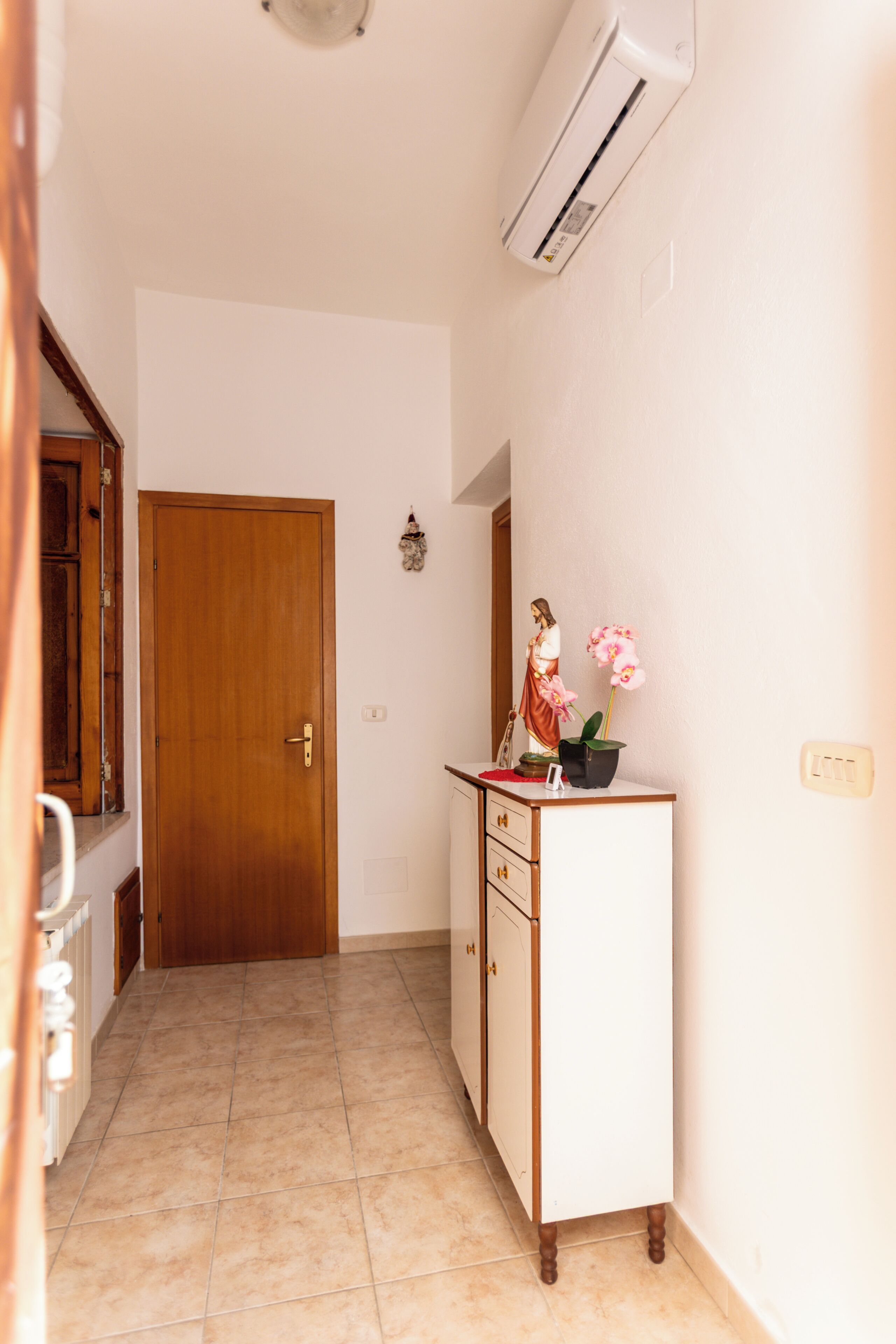 Um corredor com uma porta de madeira, um armário branco e um aparelho de ar condicionado na parede.