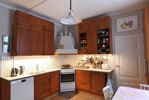 Uma cozinha com armários de madeira, bancada branca, fogão, lava-louças e luminária pendente.