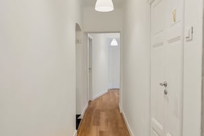 Um corredor com piso de madeira, paredes brancas e portas com placas de identificação.