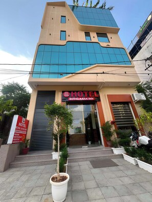 Um hotel com fachada moderna, entrada imponente e uma placa indicando ser o Royal Aana Inn.
