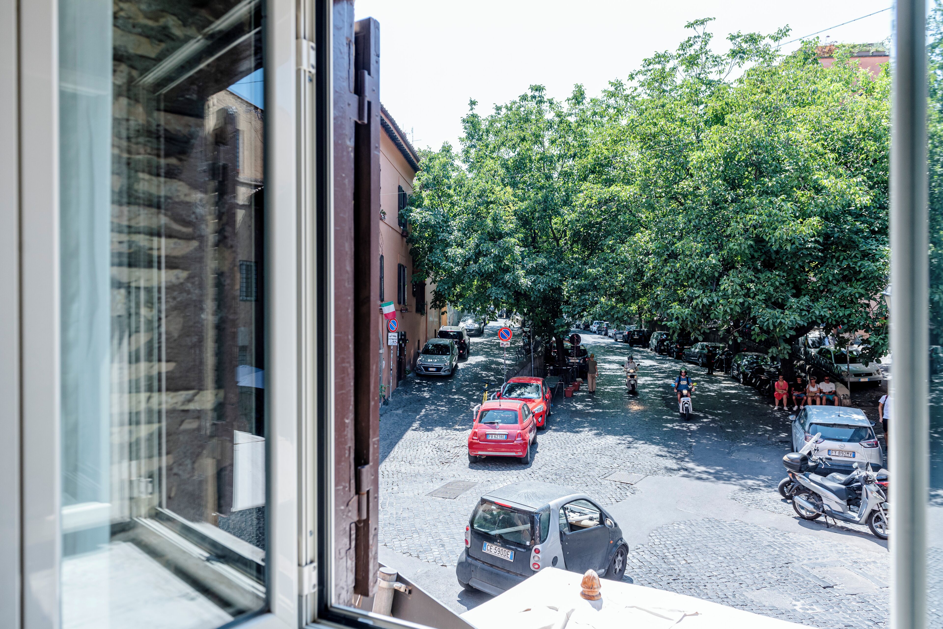 Rua de calçada com carros estacionados e uma scooter, edifícios com varandas e árvores ao longo da estrada.