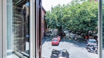 Rua de calçada com carros estacionados e uma scooter, edifícios com varandas e árvores ao longo da estrada.