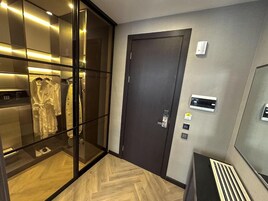 Quarto de hotel com porta de vidro deslizante que dá para um closet espaçoso, uma porta de madeira escura e um termostato fixado na parede.