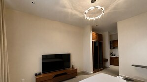 Quarto de hotel moderno com uma cama grande, uma TV em um suporte de madeira, um closet espaçoso e uma cozinha compacta.