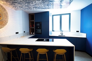 Uma cozinha moderna com uma ilha central, banquetas, forno embutido e uma janela com vista.