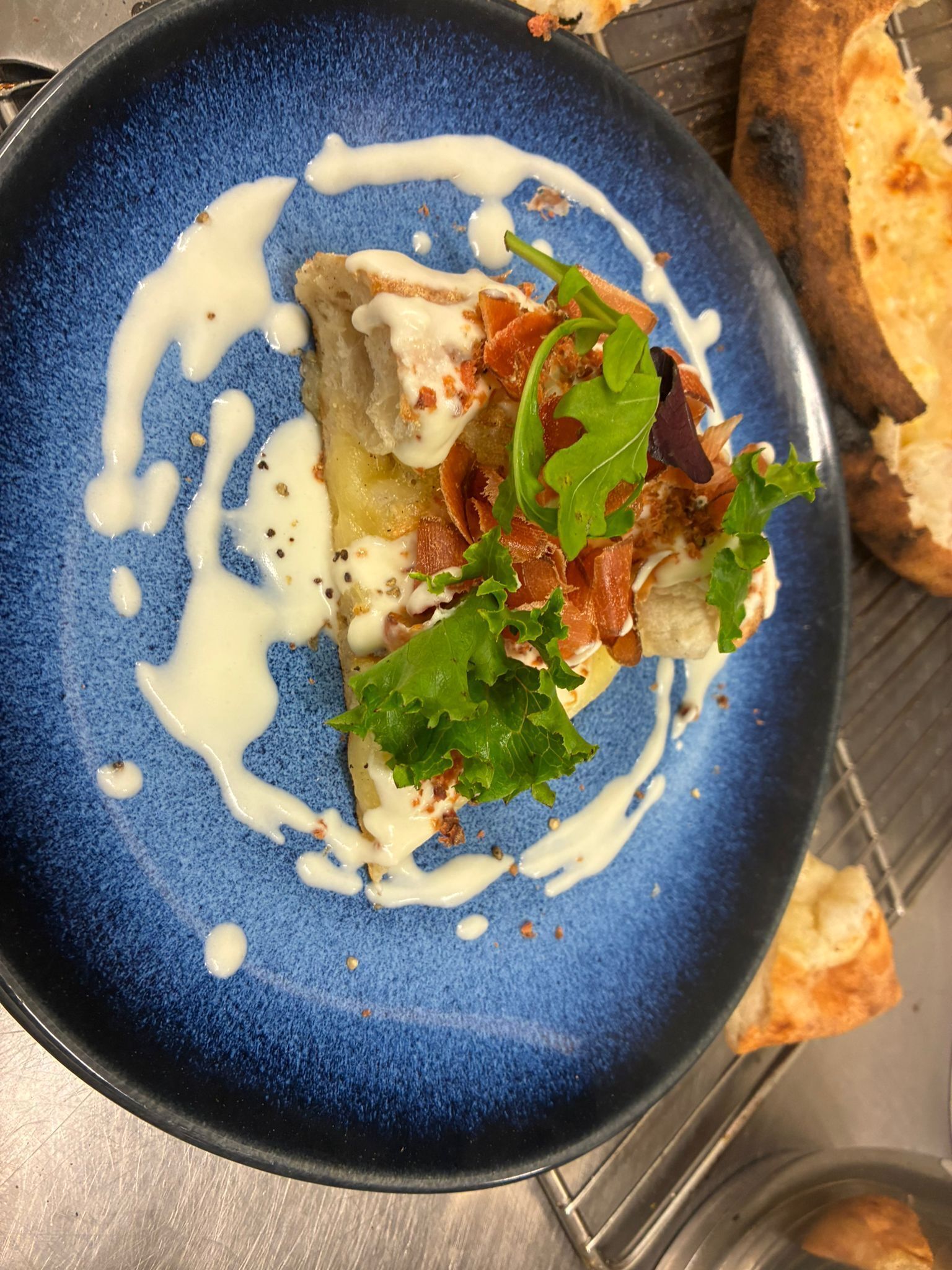 Um prato azul com um alimento, possivelmente um sanduíche ou um doce, coberto com vegetais e um molho cremoso.
