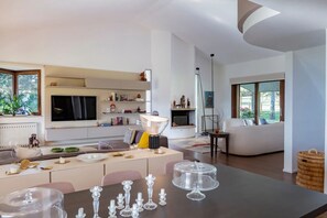 Uma sala de estar moderna com área de jantar, lareira e uma janela grande.
