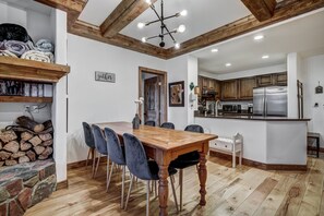 Uma área de refeições com mesa e cadeiras de madeira, uma cozinha com eletrodomésticos modernos e um mezanino com teto de madeira.