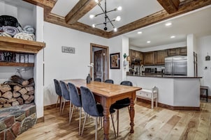 Uma área de refeições com mesa e cadeiras de madeira, uma cozinha com eletrodomésticos modernos e um mezanino com teto de madeira.